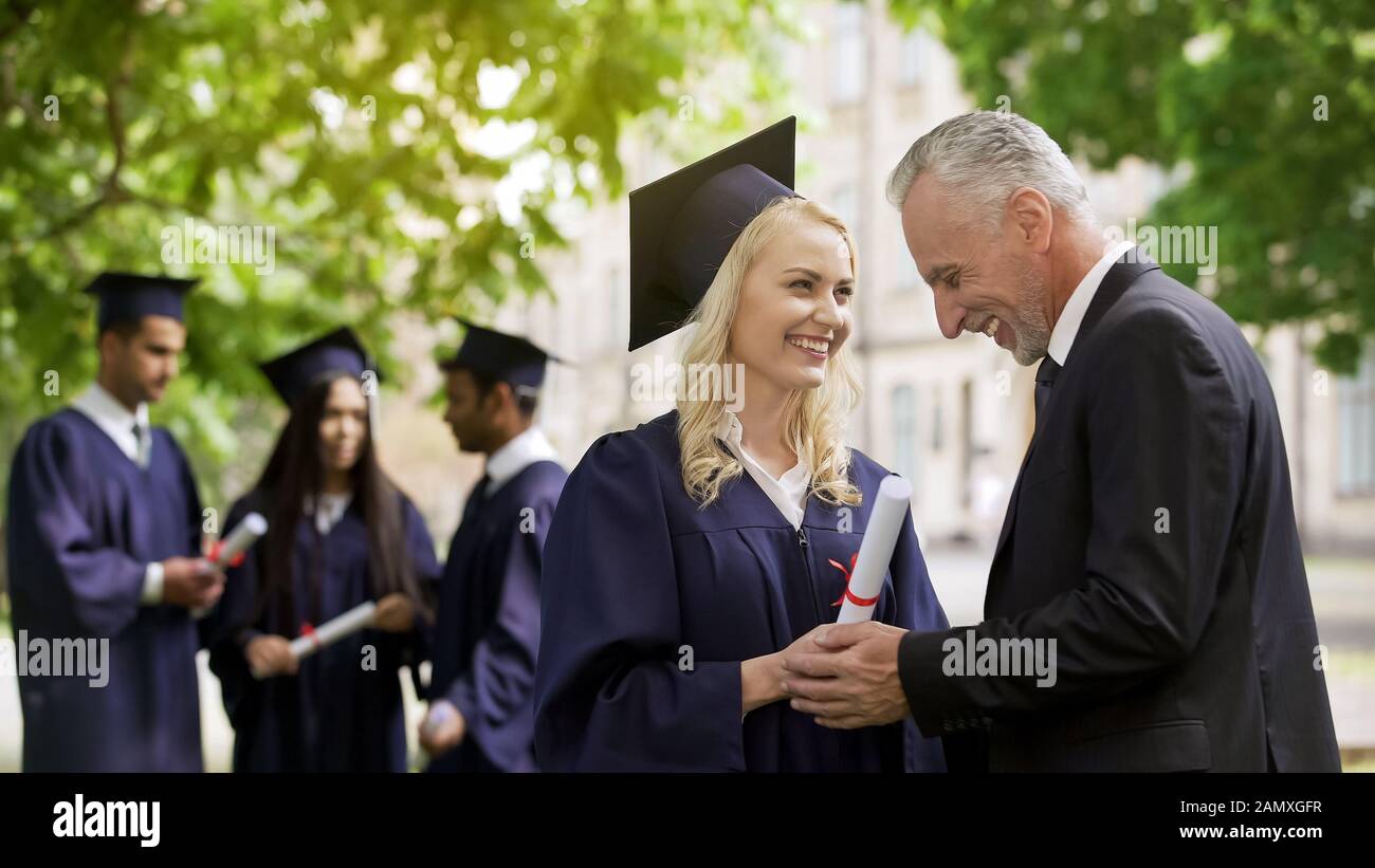 Happy father congratulating graduate daughter holding her hands near ...