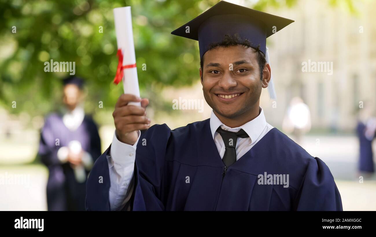 Charming Hispanic graduate smiling and showing diploma for camera ...