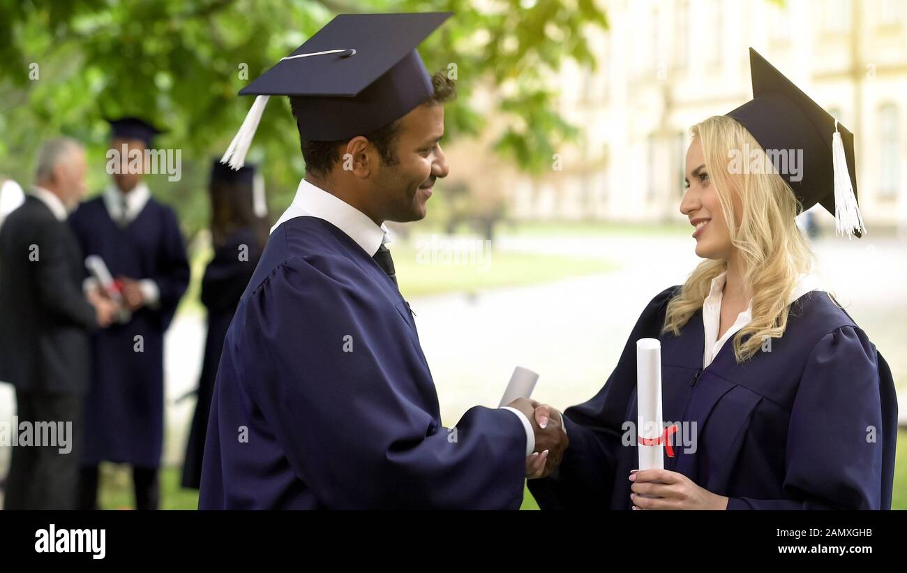 Students in graduation gown with diplomas talking, shaking hands and ...