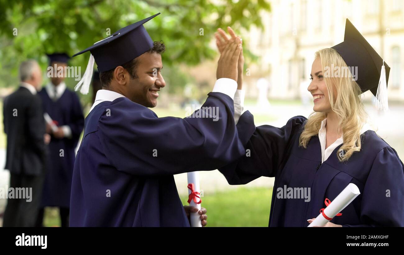 Graduate students with diplomas talking, high-fiving each other ...