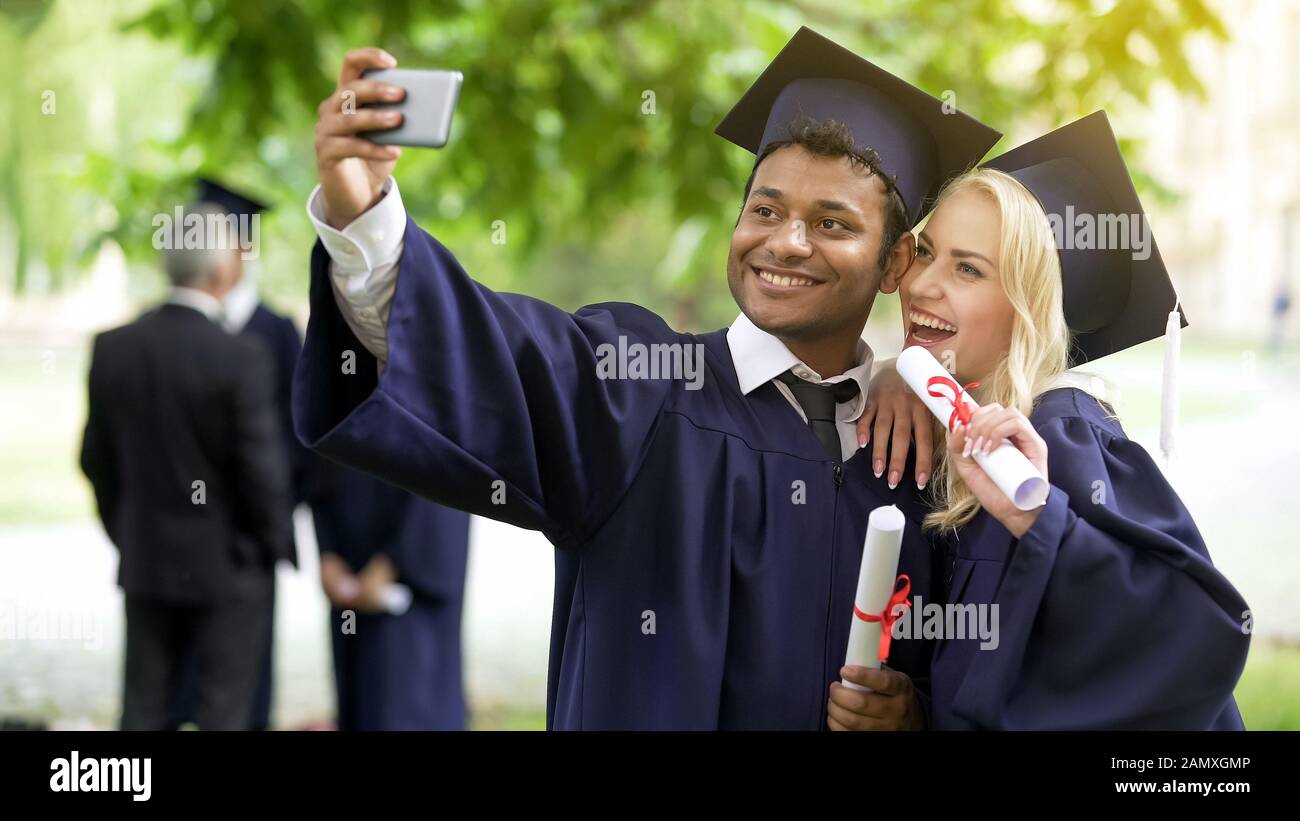 Young people in graduation outfit taking selfie with mobile phone ...