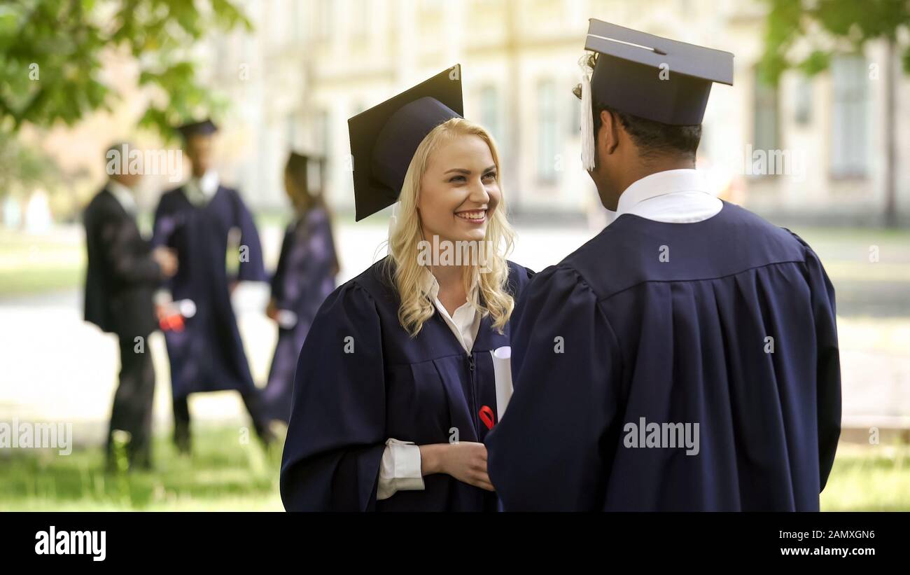 Female graduate in square hat with diploma talking to classmate ...
