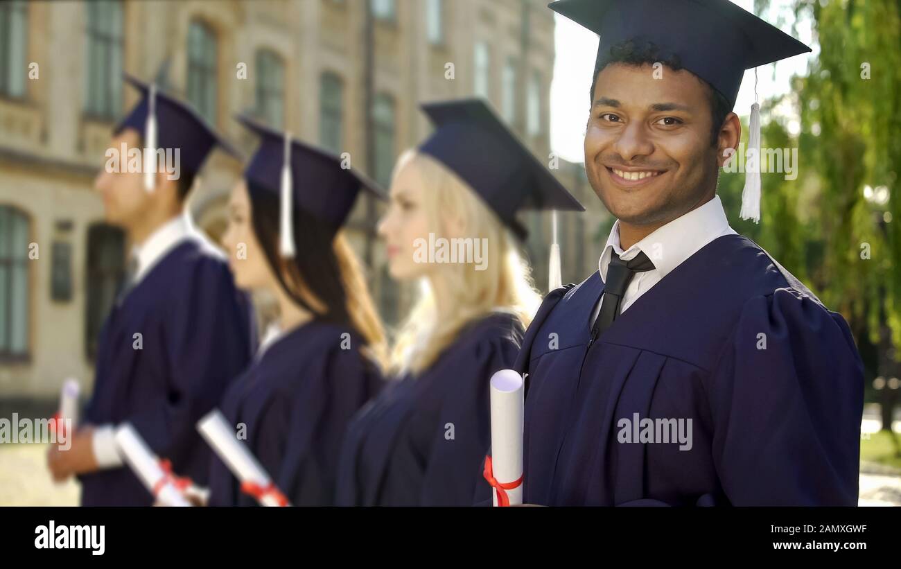 Mixed-race graduate student with diploma smiling into camera, exchange ...