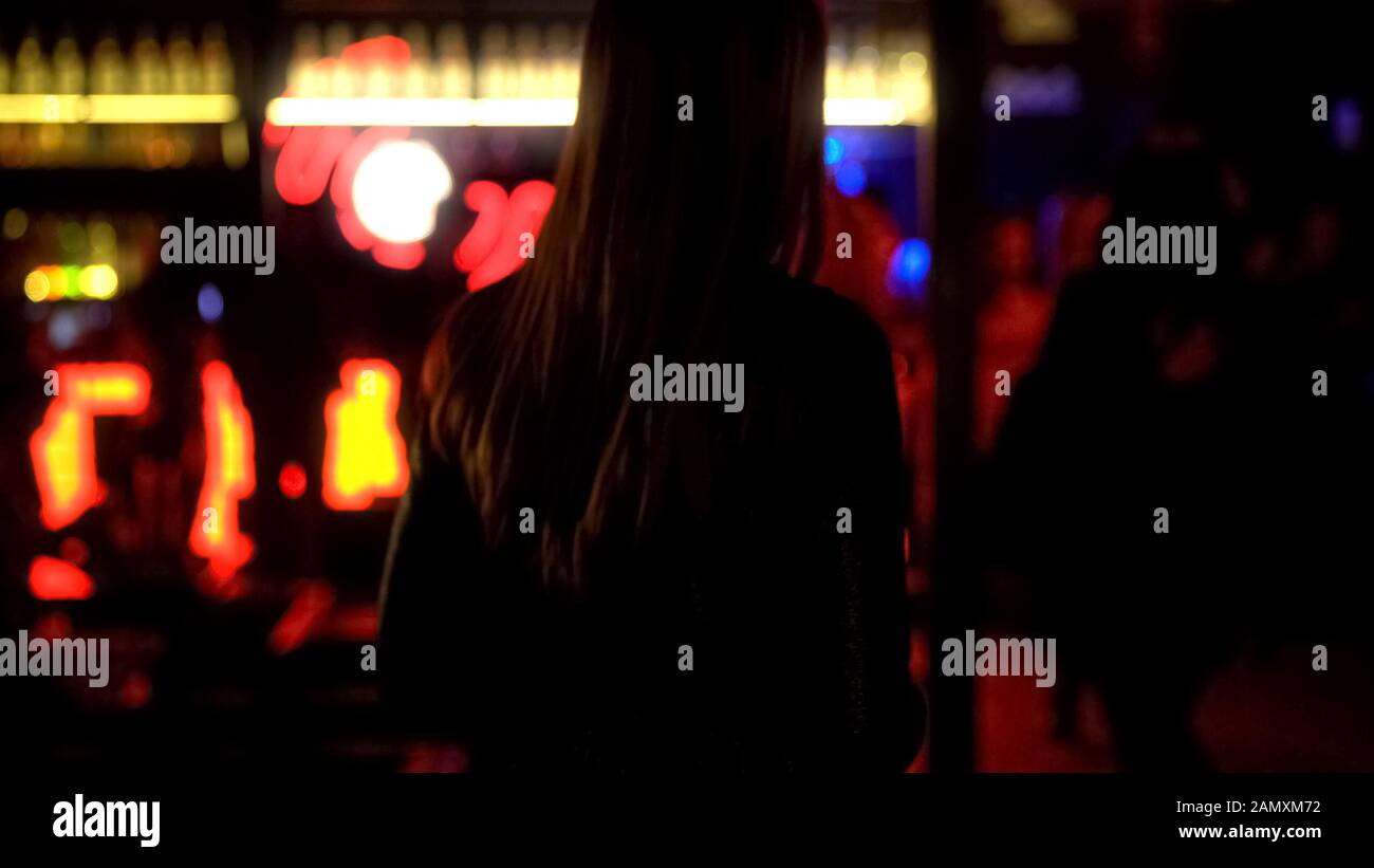 Beautiful long-haired woman waiting for friends at night club, back ...