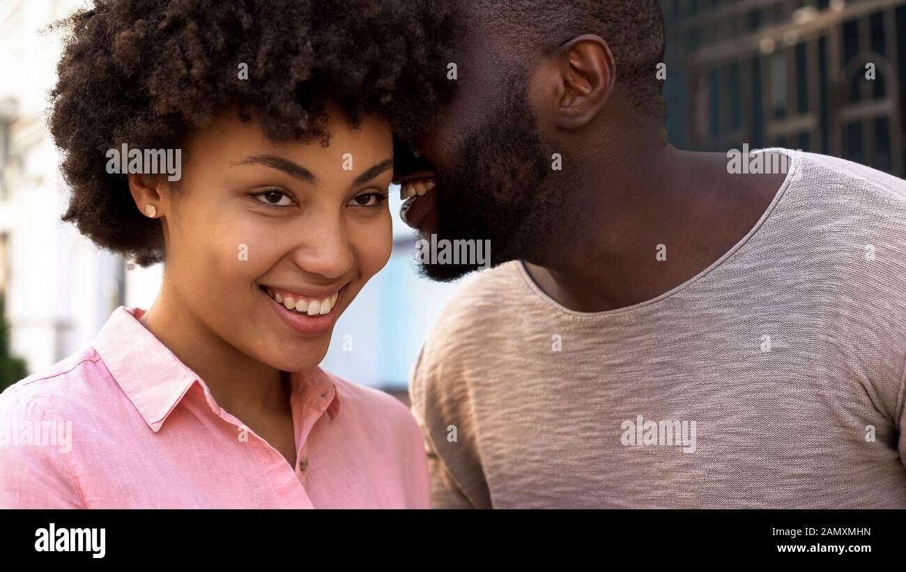 African boyfriend whispering words of love to girlfriend, happy smiling ...