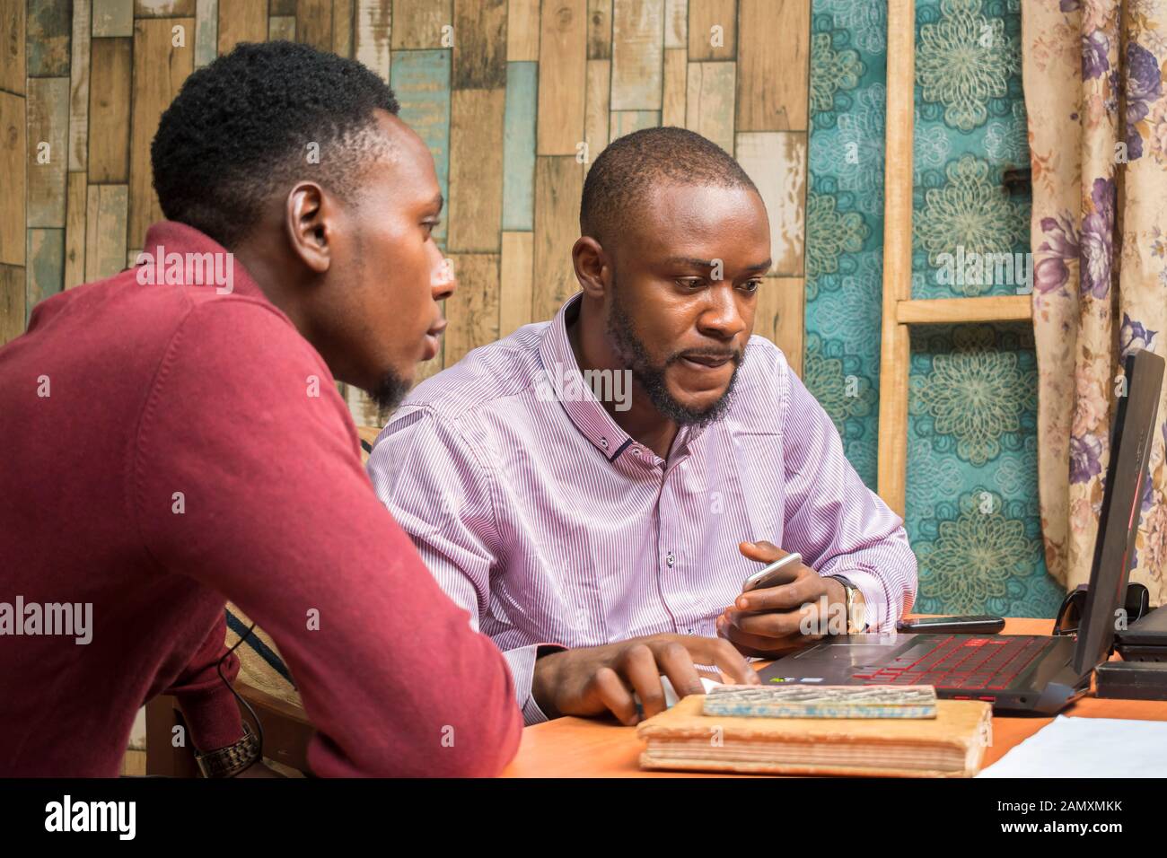 two young black people working together in an office, looking at laptop ...