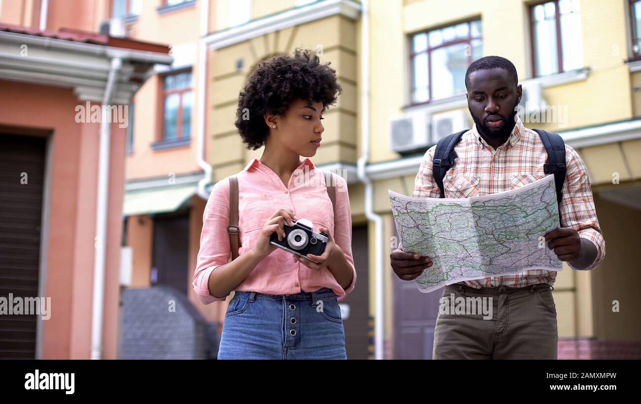 Black couple of tourists with map and photo camera, choosing direction ...
