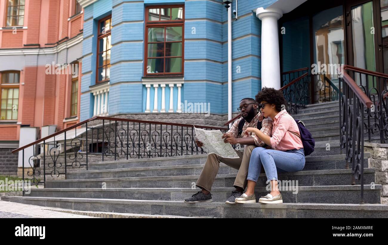 University students looking at map, sitting on building stairs ...
