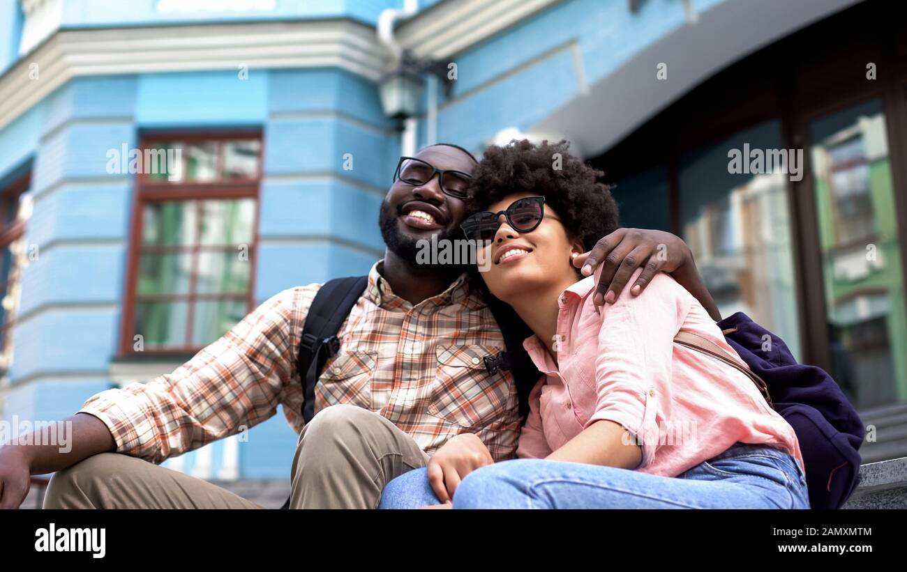 Afro-american student couple hugging, sitting on university building ...