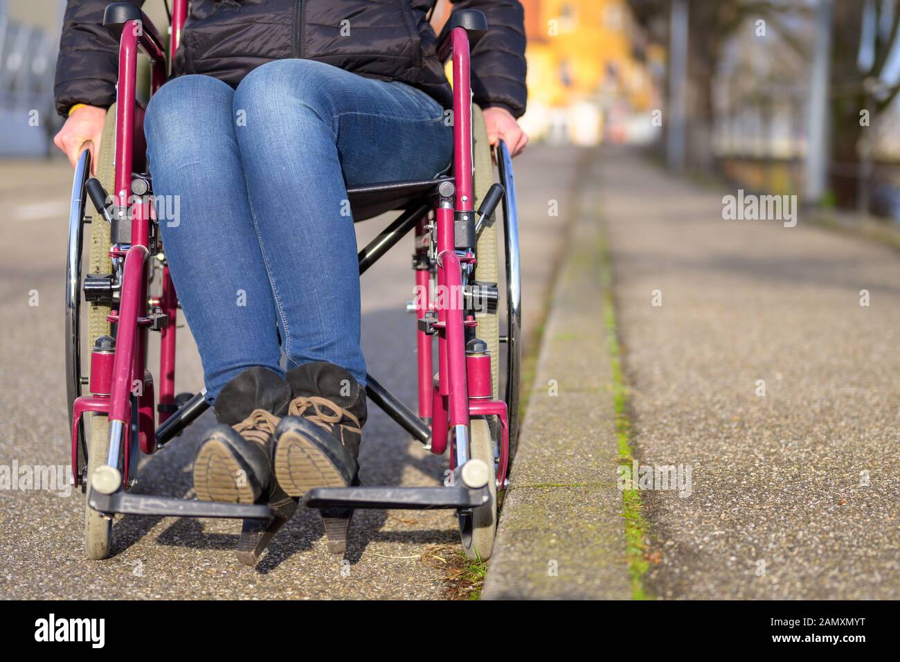Feet of a disabled woman seated in a wheelchair at the edge of an urban ...