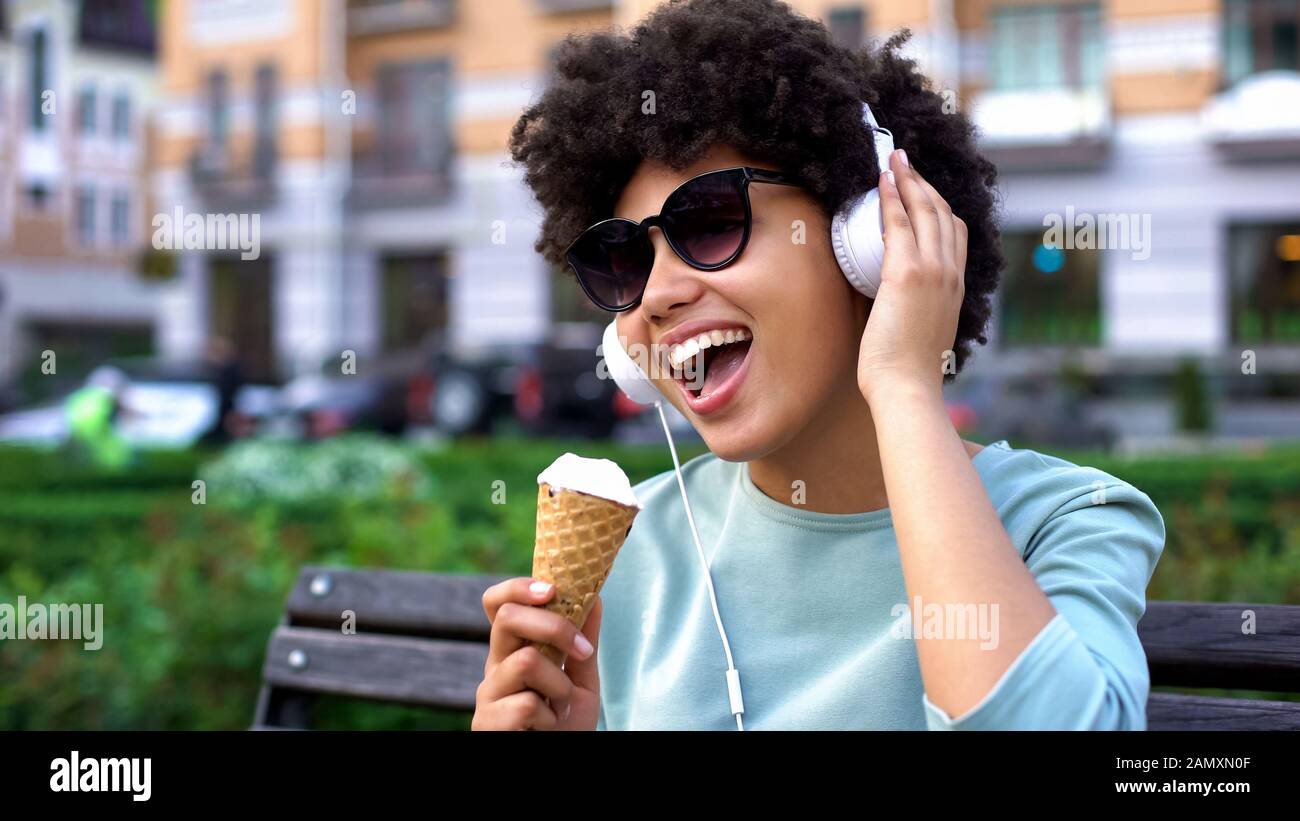 Afro-american woman enjoying music in headphones, eating ice-cream on ...