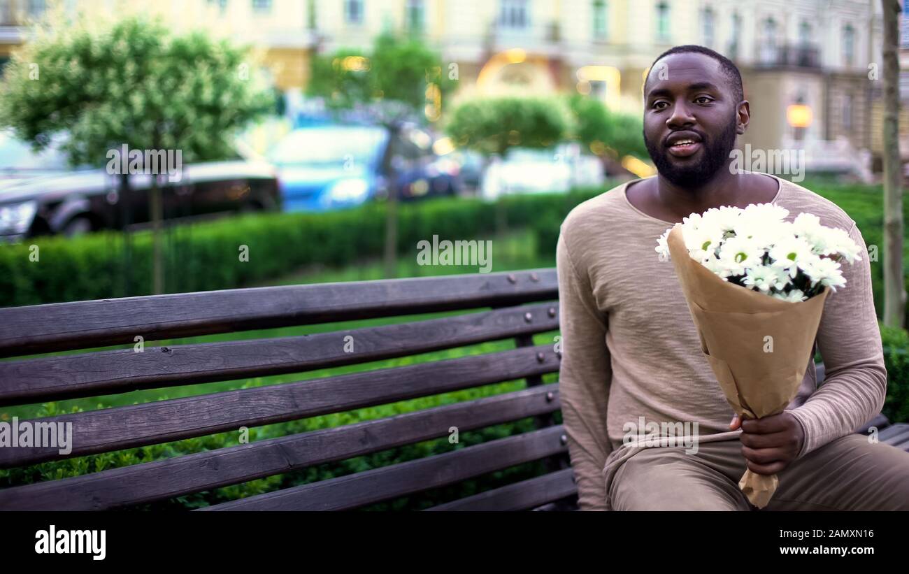 Black man with flowers sitting on bench, waiting for girlfriend ...