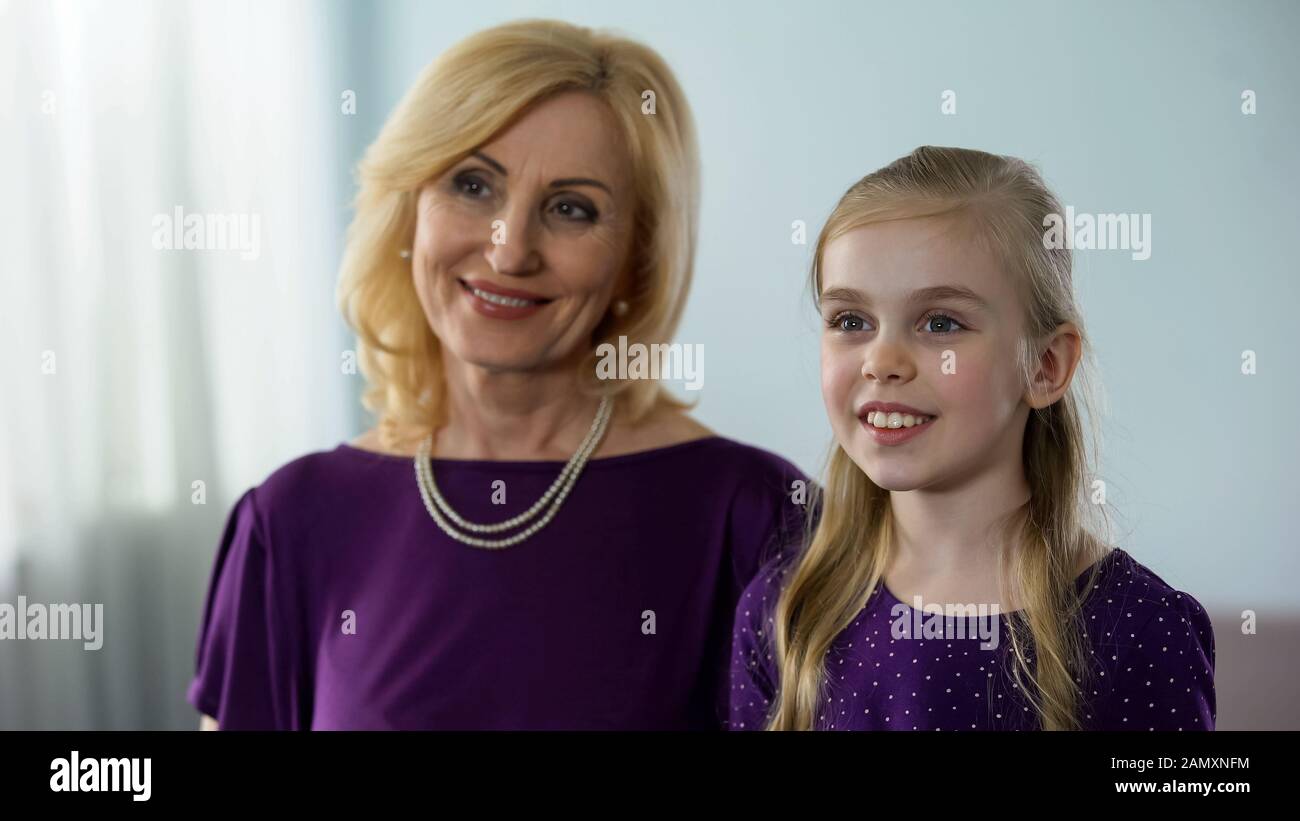 Pretty granddaughter and her granny smiling in front of mirror ...