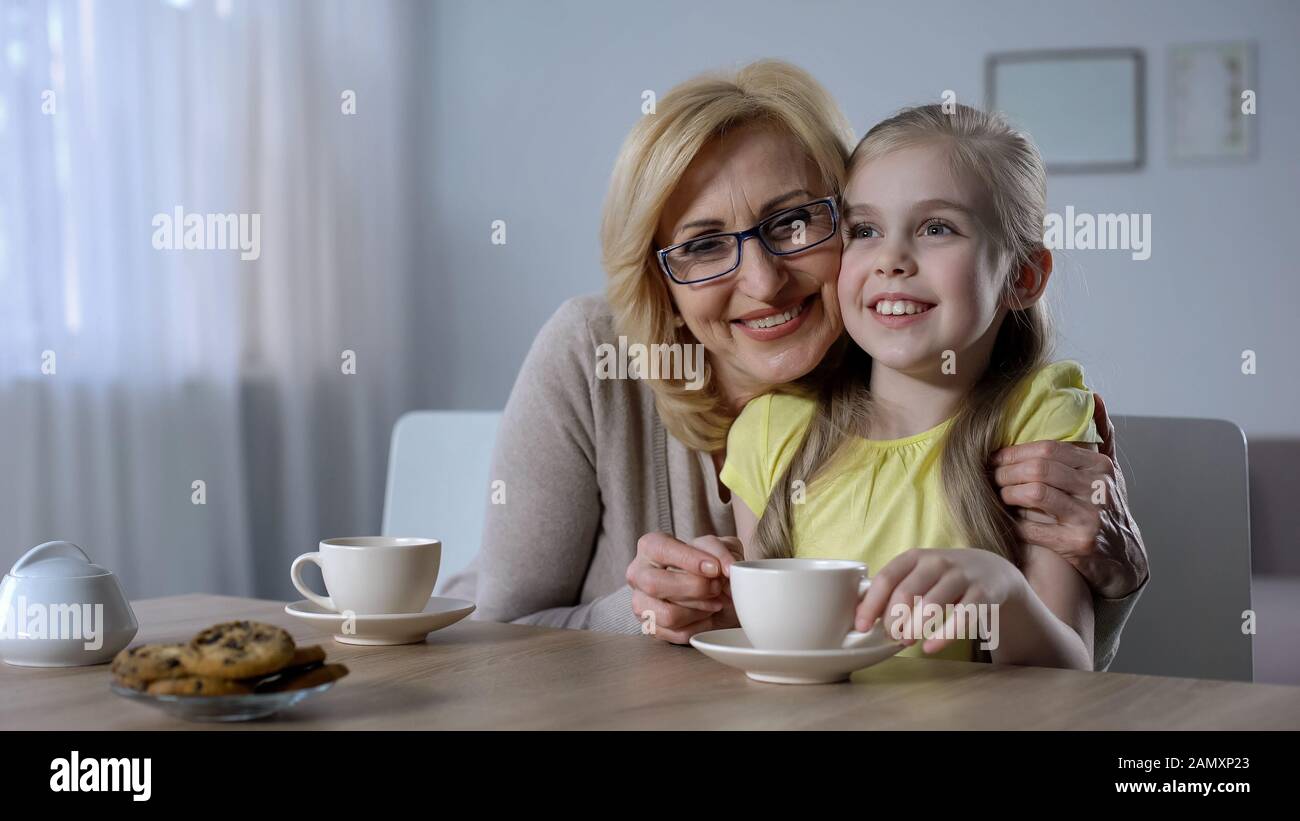 Loving grandma drinking tea with cute granddaughter, tightly hugging ...