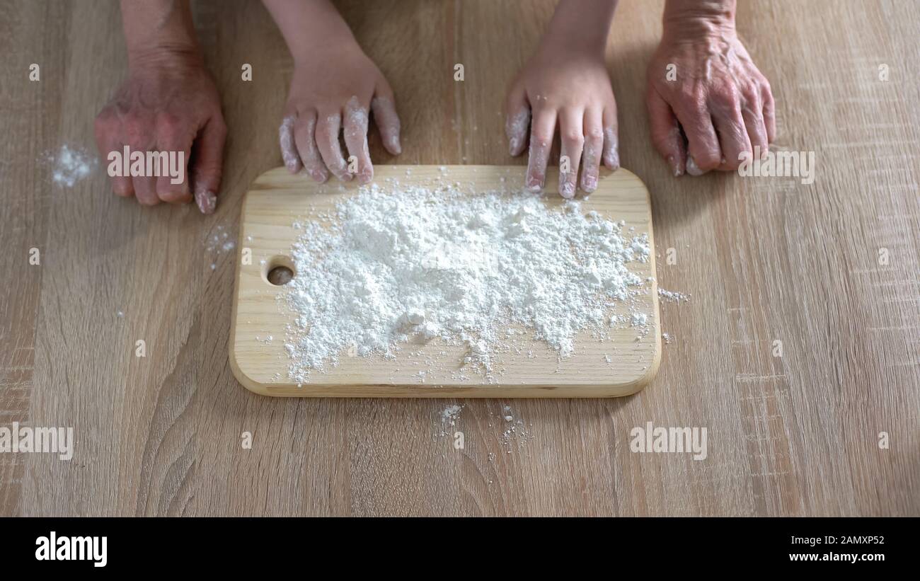Hands of grandmother and granddaughter pouring flour on plank, cooking ...