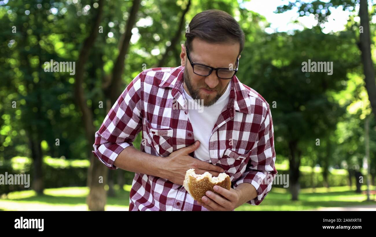 Man with burger in hand feeling nausea, junk food poisoning, body ...