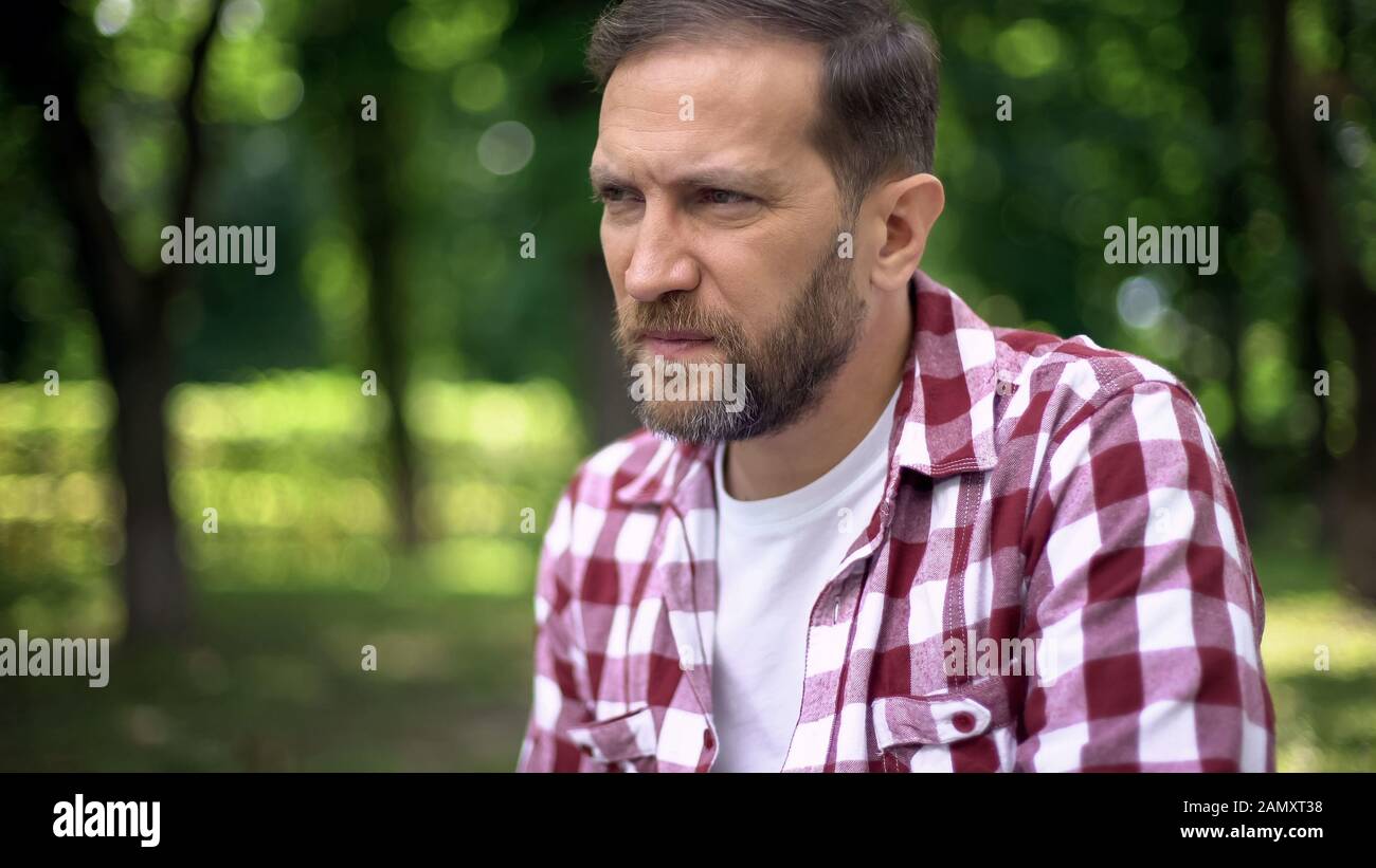 Concerned man sitting on bench in park, thinking of life difficulties ...