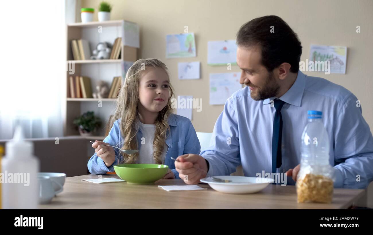 Friendly daughter and dad eating cereal with milk, breakfast, healthy ...
