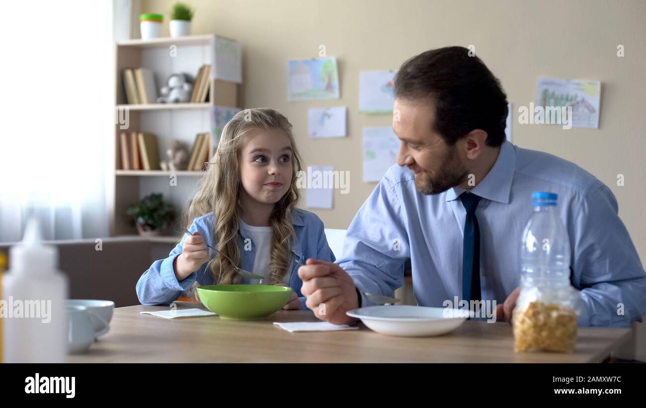 Happy little girl and father eating cornflakes at breakfast, family ...