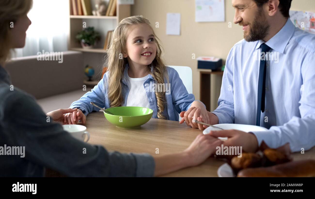 Smiling family praying before eating breakfast together, morning ritual ...