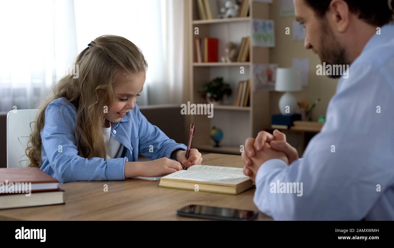 Smart daughter writing in exercise book, caring daddy is proud of his ...