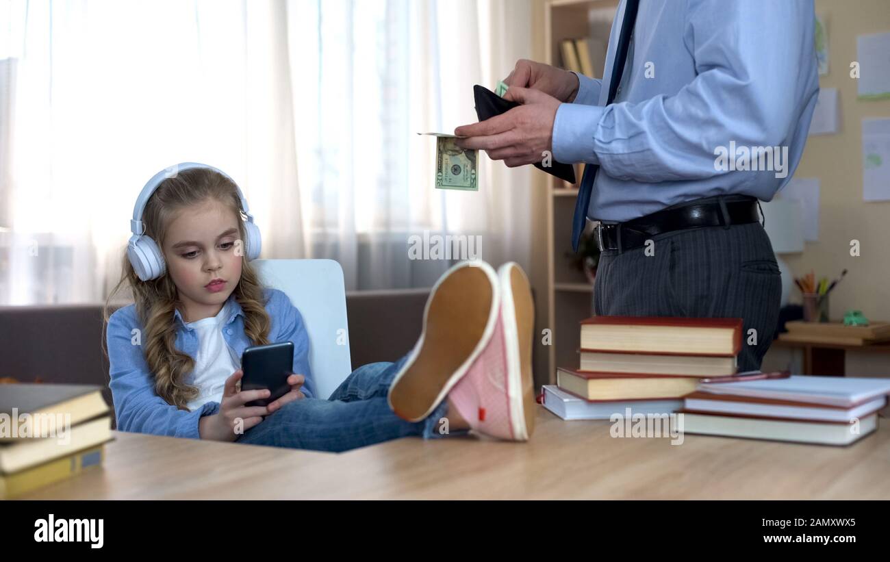 Father in suit giving pocket money to daughter listening to music in ...