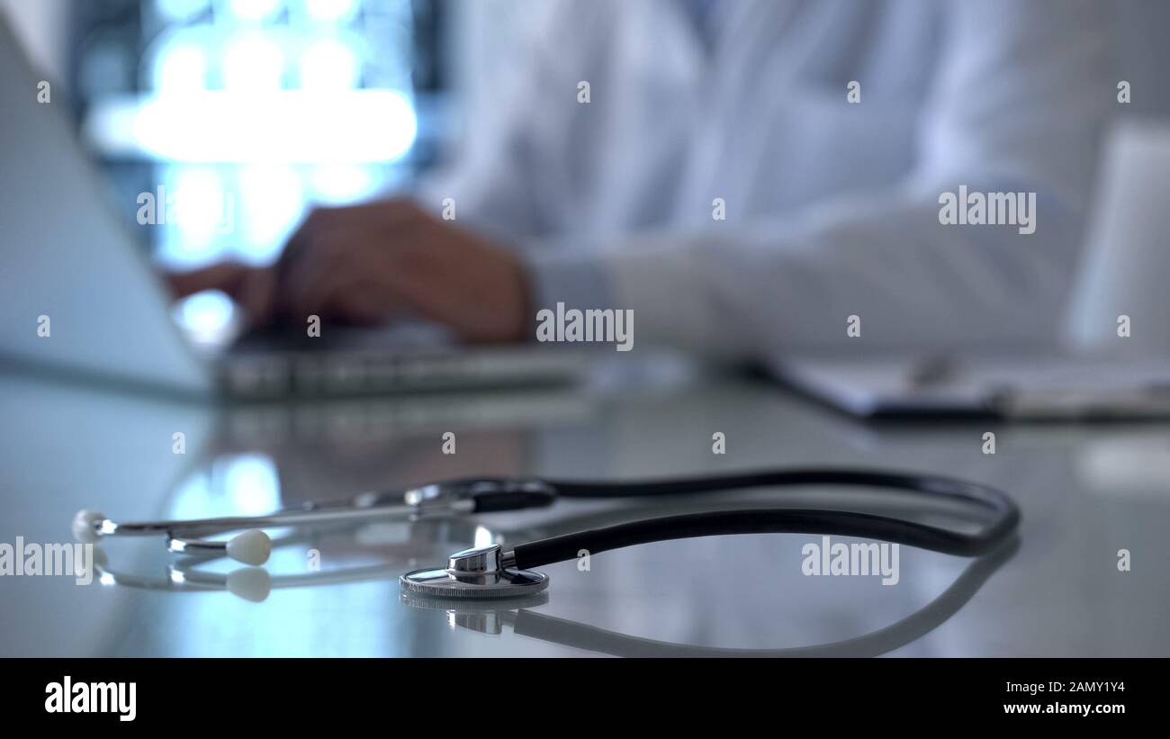 Professional doctor working on laptop in lab, stethoscope on table ...