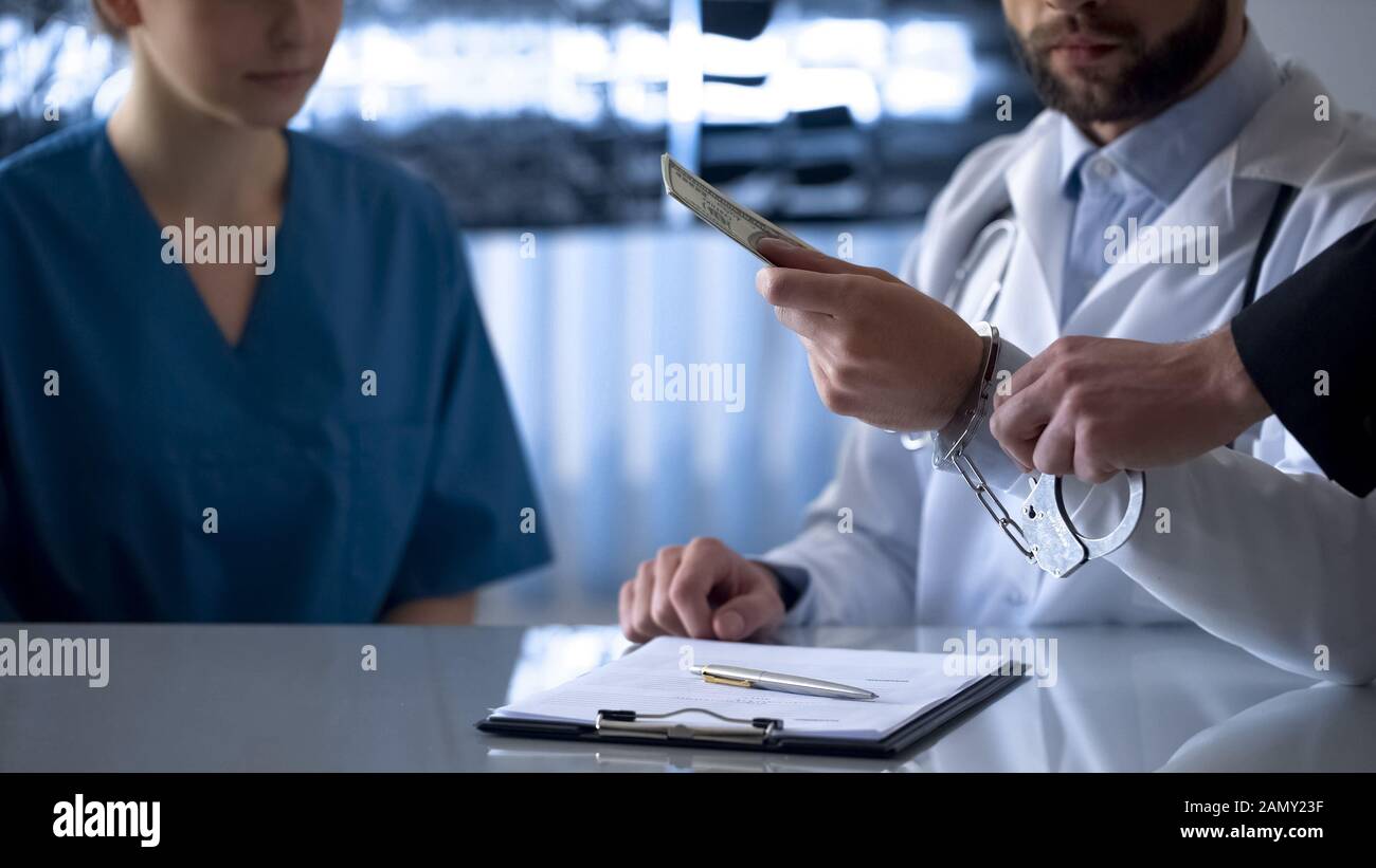 Policeman putting handcuffs on corrupt doctor taking bribe from intern ...