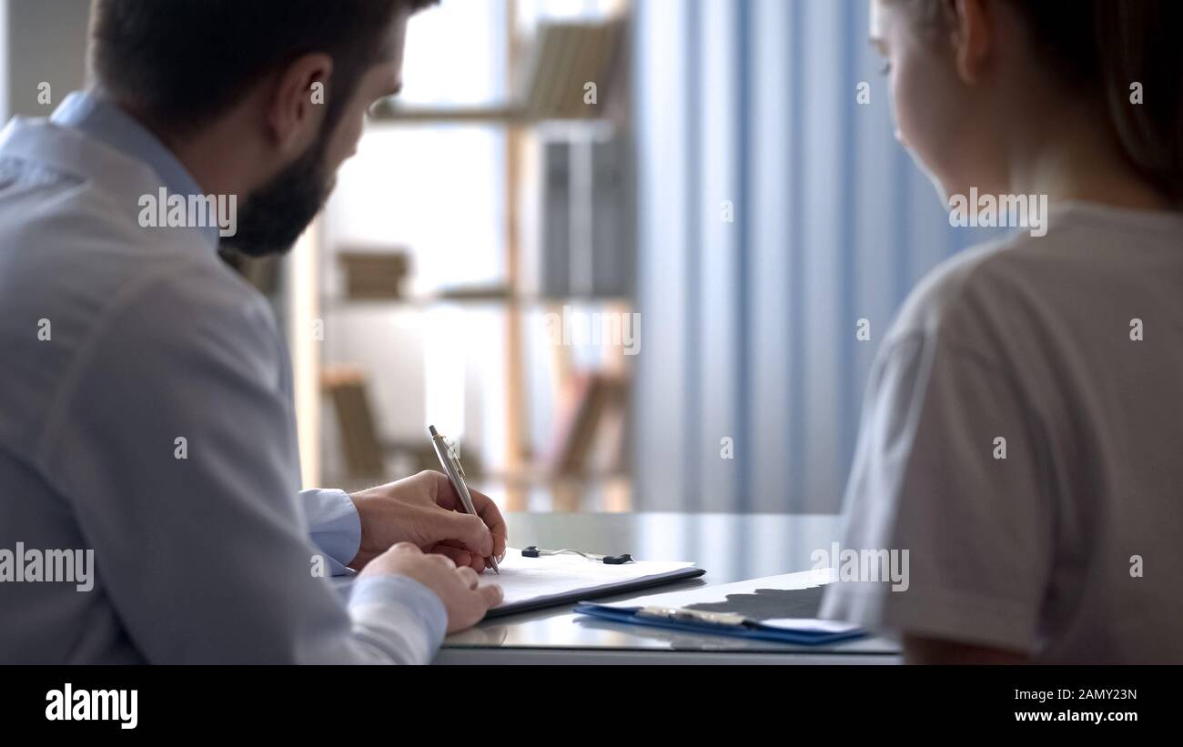 Therapist writing medical receipt to young female patient, health and ...
