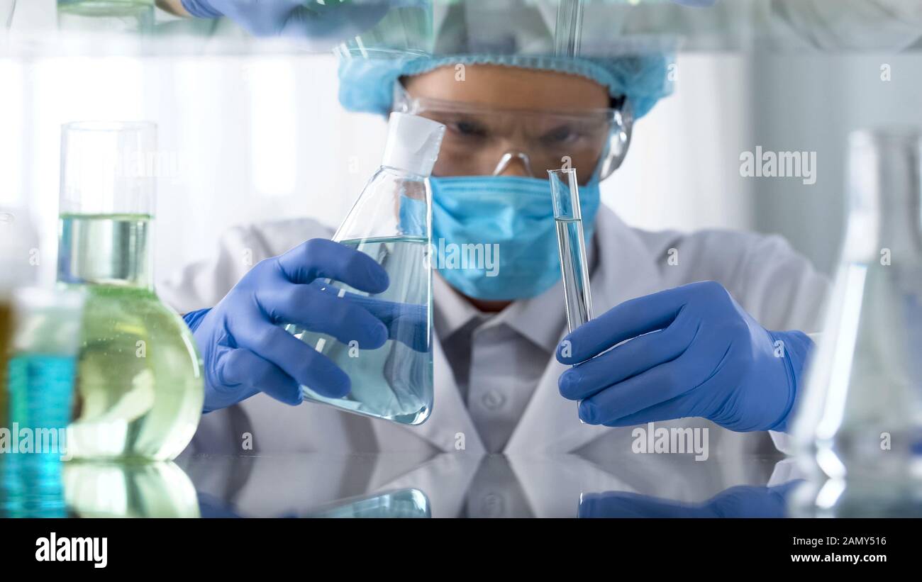 Lab worker examining test tube with liquid before mixing reagents ...