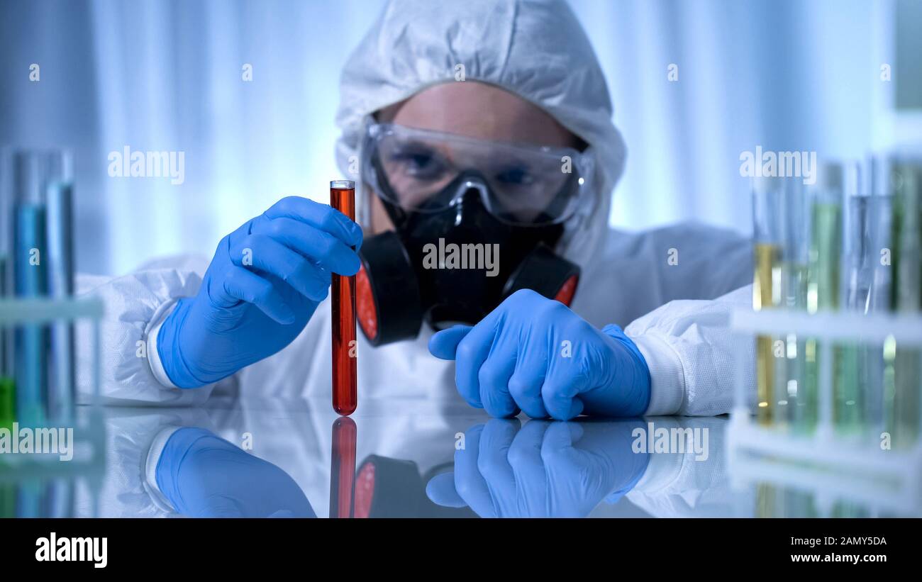Scientist in gas mask holding test tube with dangerous substance ...