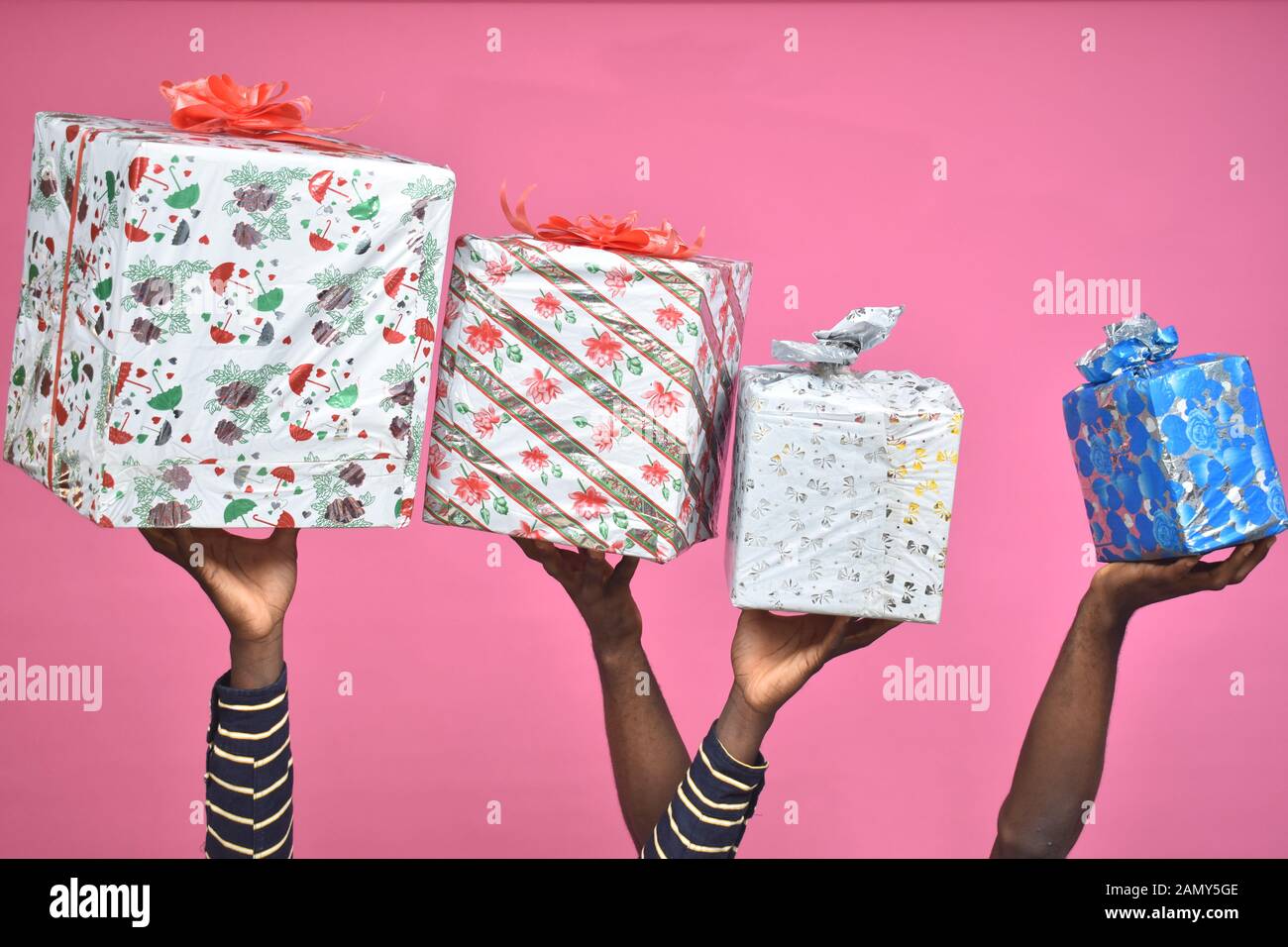 two people holding presents up, hands only, over plain pink background ...