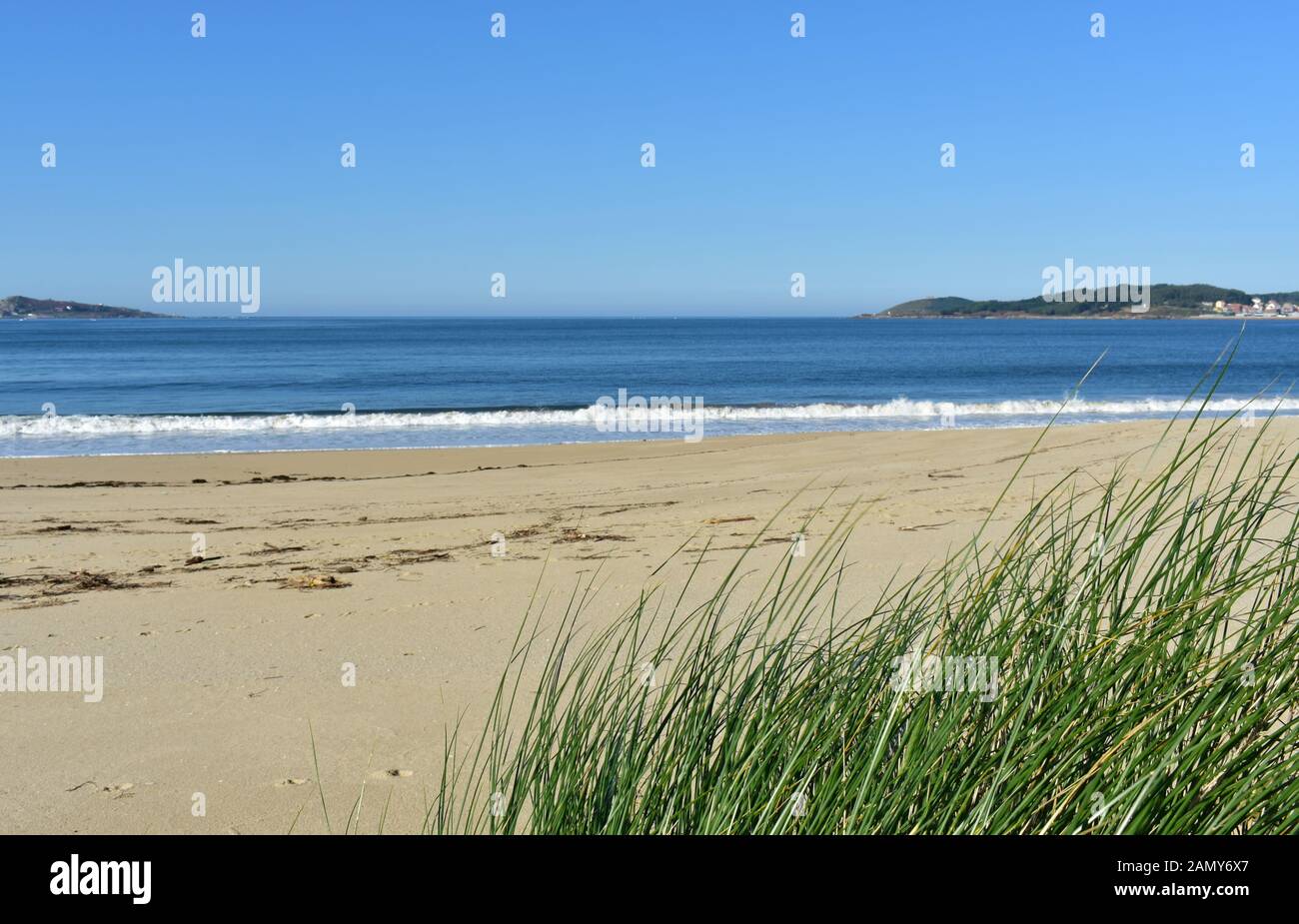 Beach with grass on sand dunes, blue sky and sea with small waves ...