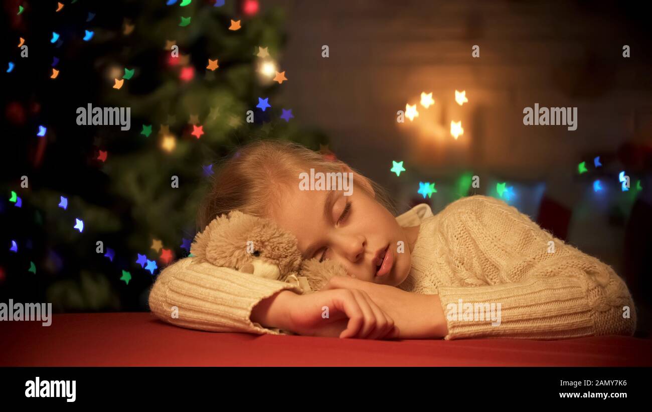 Cute girl falling asleep on table, hugging teddy bear, X-mas tree ...