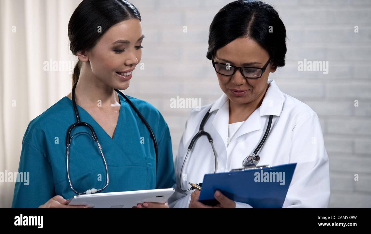 Nurse checking data in tablet, speaking with doctor, discussing ...