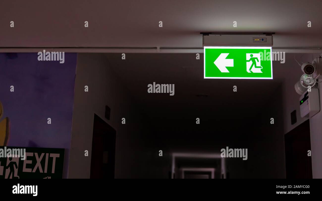Emergency exit green sign hanging by the ceiling inside a hotel alley ...