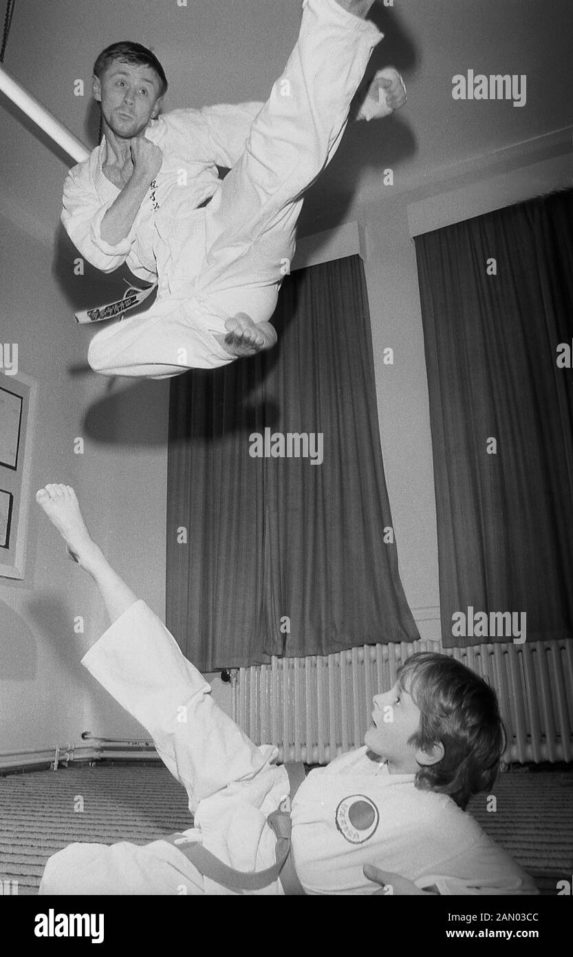1980s, historical, young boy practising a karate kick with a male ...