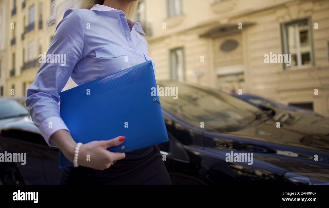 Pretty businesswoman walking along street to office, holding documents ...