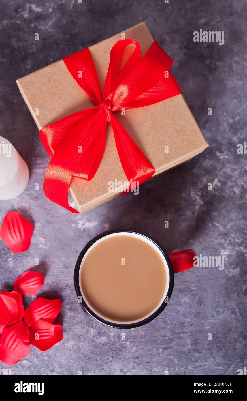 Red mug of coffee, gift box and red rose petals on the gray table. Top ...