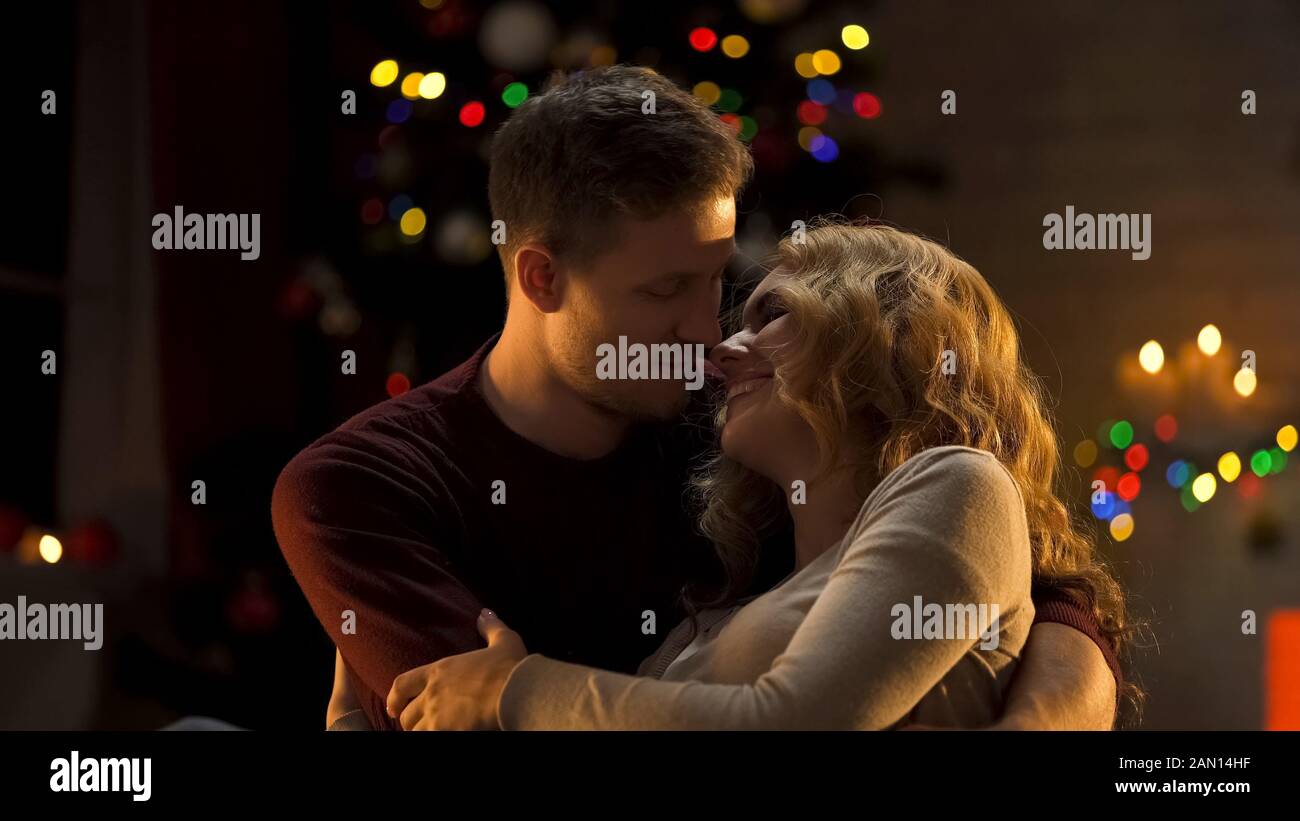 Loving couple embracing tenderly under Christmas tree, first holiday ...