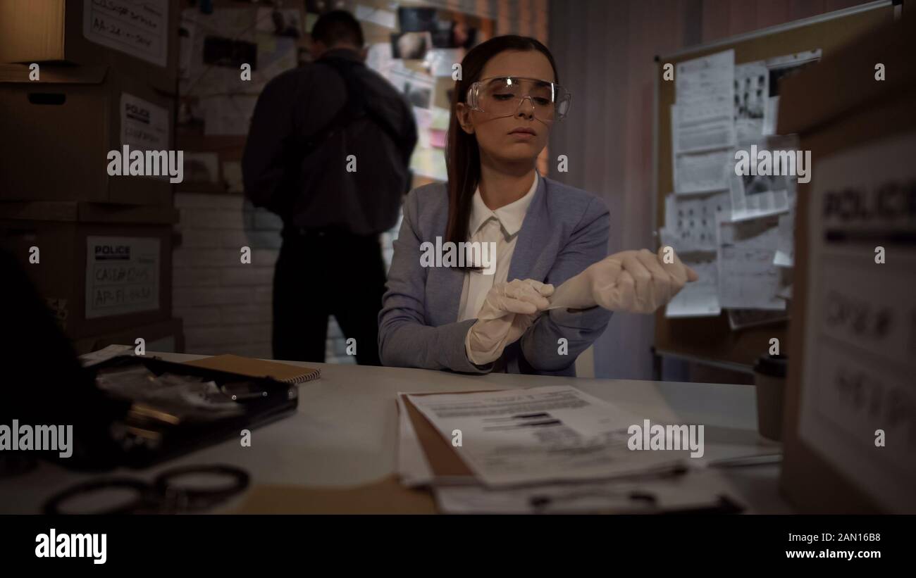 Female Criminologist Putting On Gloves To Examine Evidence