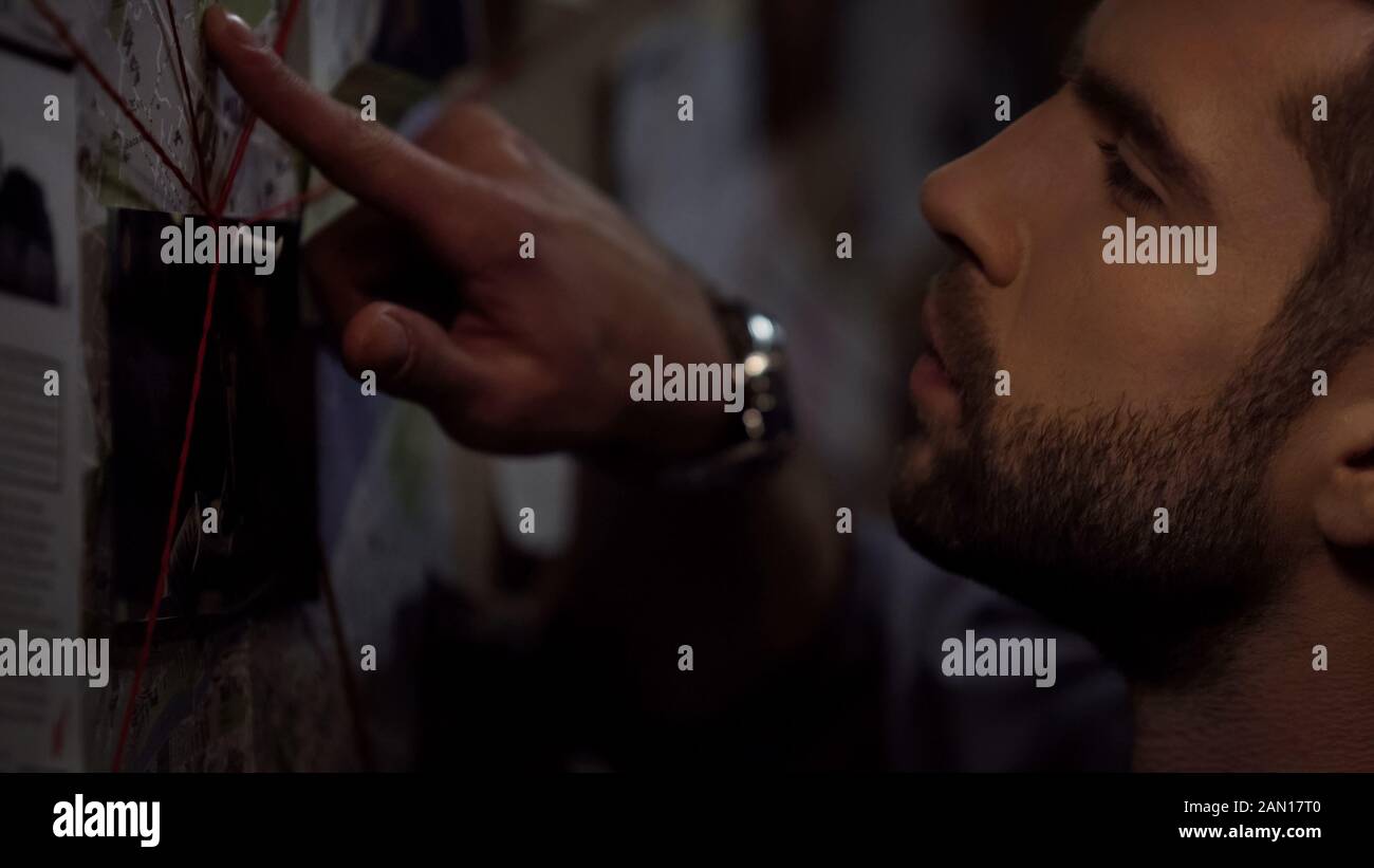 Concentrated detective marking criminal events on board with red string ...