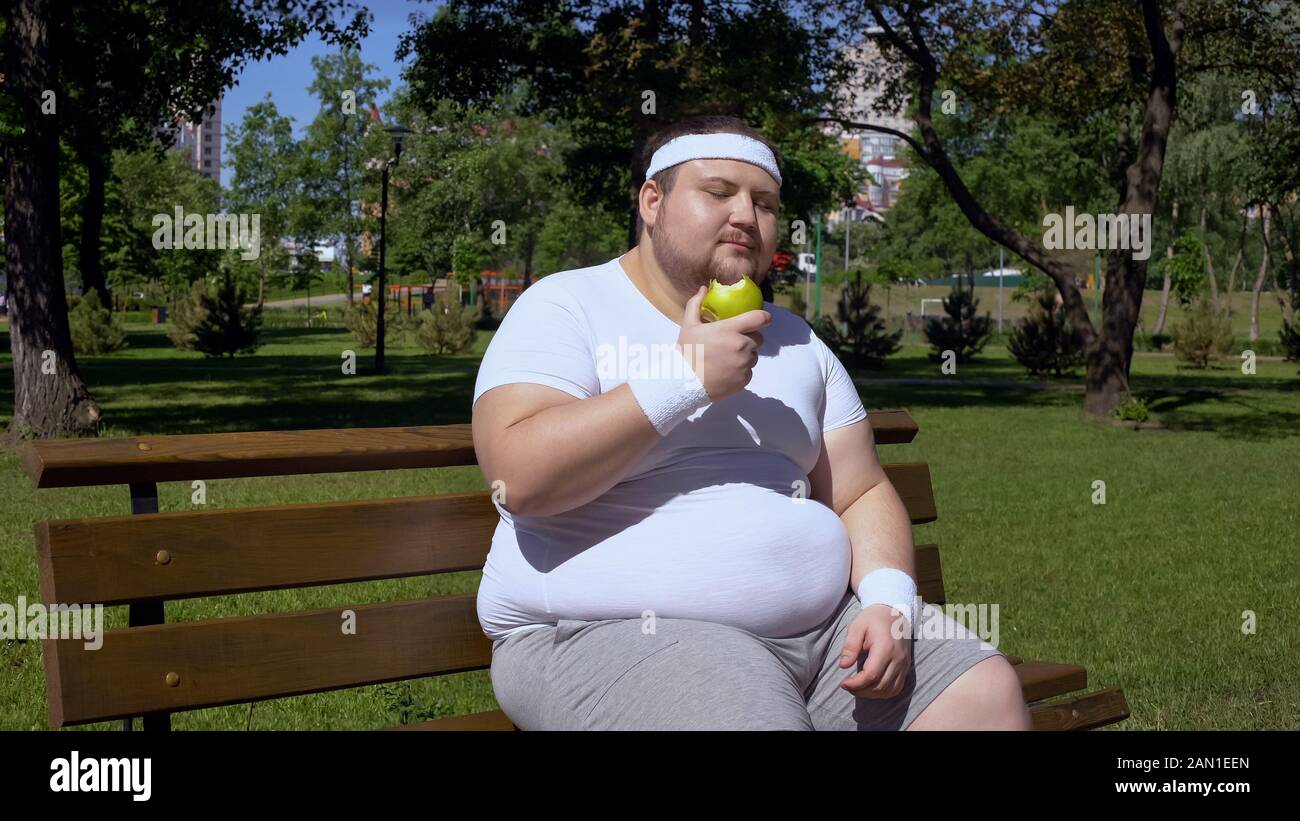 Fat young man eating apple after jogging outdoors, proper lunch with ...