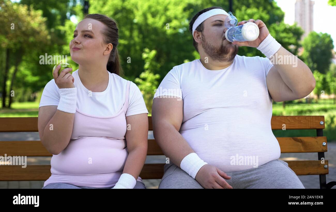 Fat couple on bench, man drinking water, woman eating apple, healthy ...