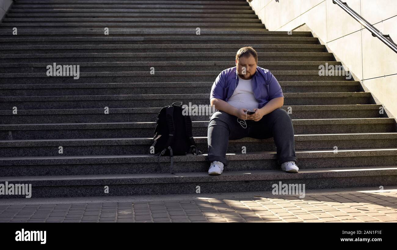 Fat man listening to music on stairs, loneliness, overweight causes ...