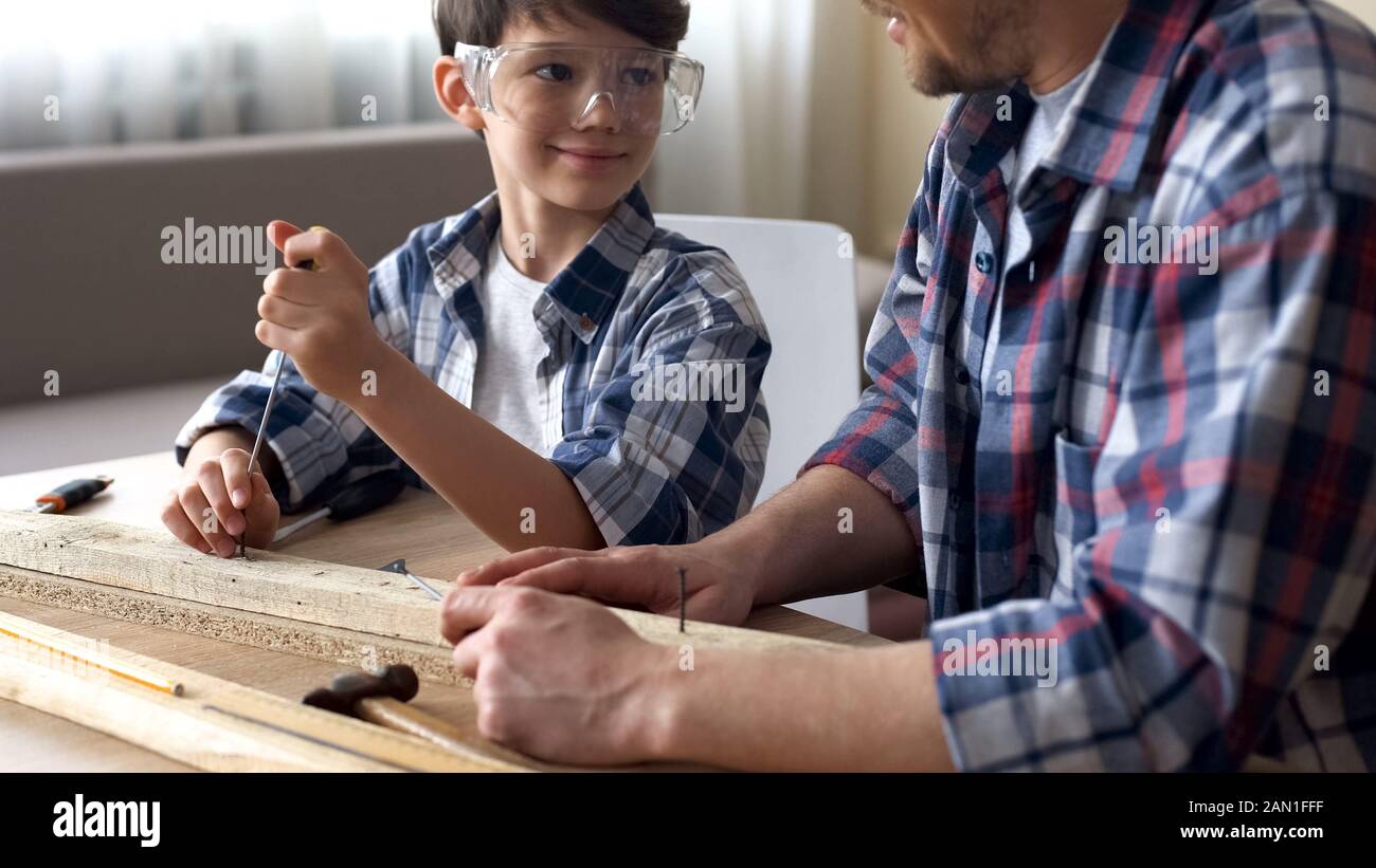 Smart attentive boy working with screwdriver and wood, father teaching ...