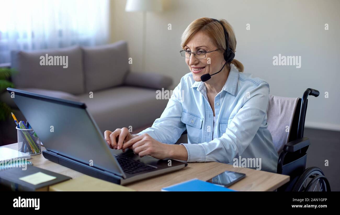 Disabled female manager sitting at office desk, working on laptop from ...