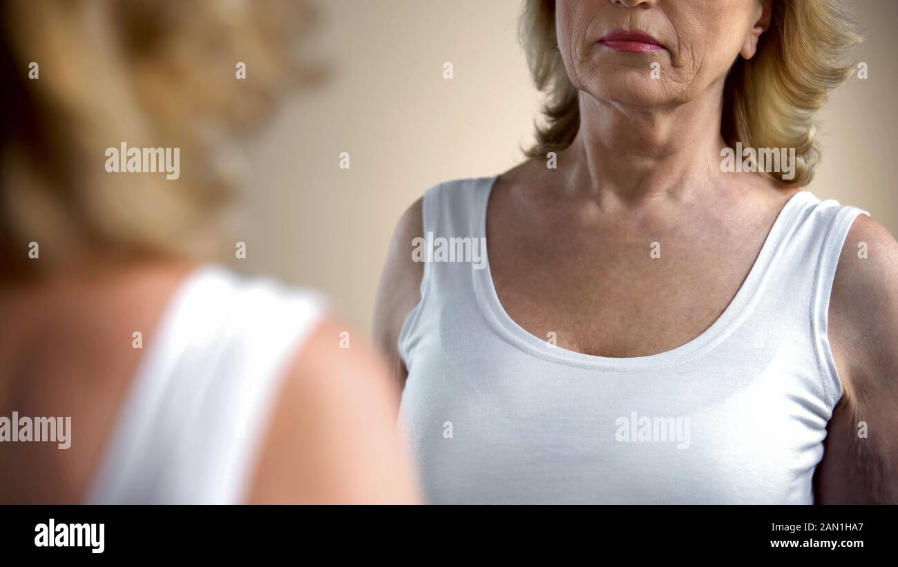 Unsatisfied senior woman looking in mirror at her wrinkled body, aging ...