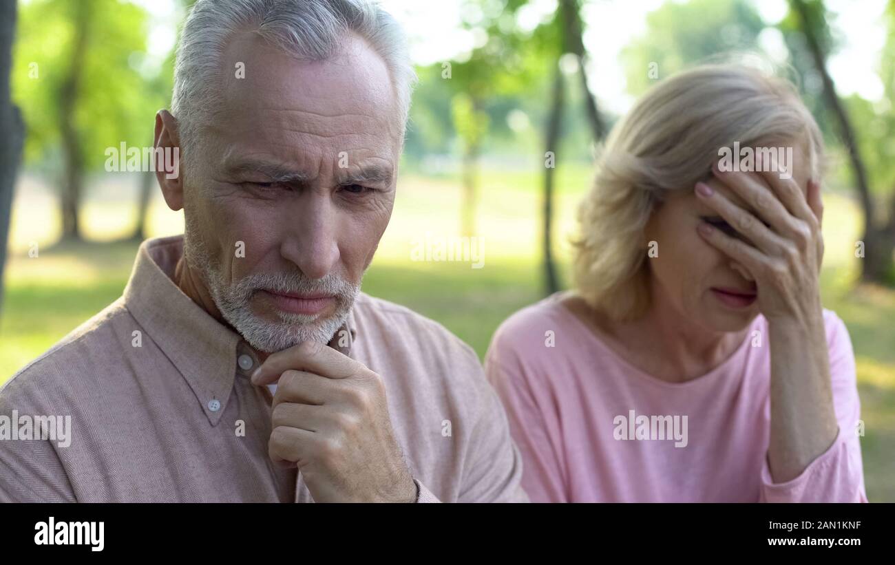 Senior man feeling sad and guilty, wife crying sitting apart, couple ...