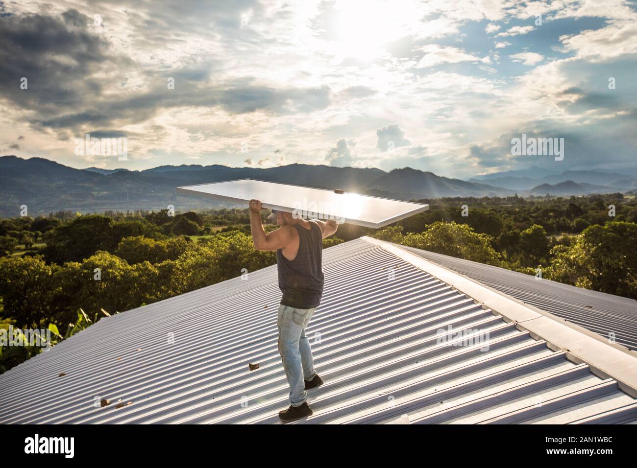 Construction worker carries solar panel above head on roof Stock Photo ...